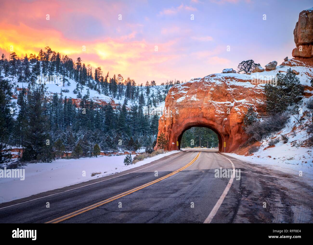 Road with tunnel through red rock arch in snow, at sunset, Highway 12 ...