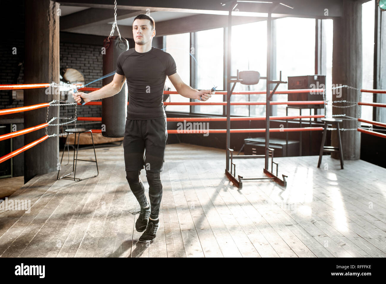 Young athletic man in black uniform training with a jumping rope ...