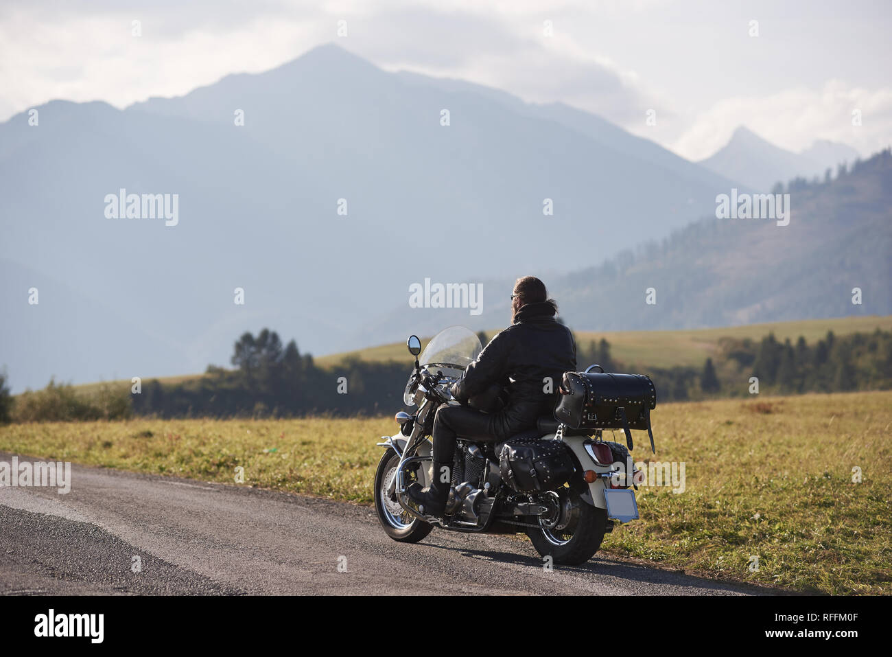 Back view of biker in black leather jacket riding cruiser motorcycle ...