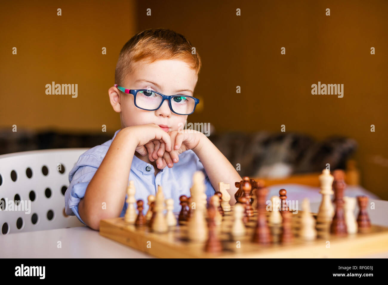 Little baby boy with down syndrome with big blue glasses playing chess ...