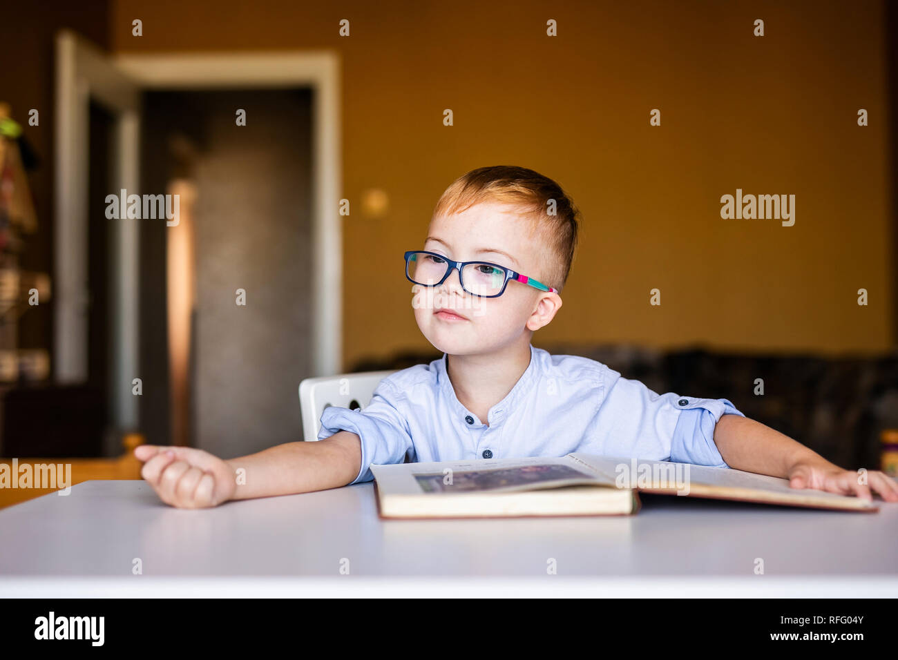 Cute toddler boy with down syndrome with big glasses reading intesting ...