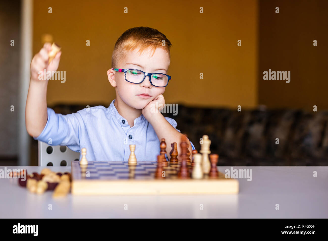 Ginger boy with down syndrome with big glasses playing chess at home ...