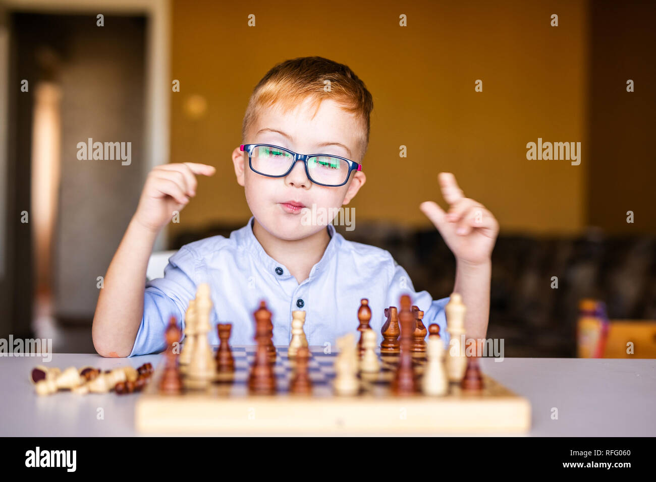 Ginger boy with down syndrome with big glasses playing chess at home ...