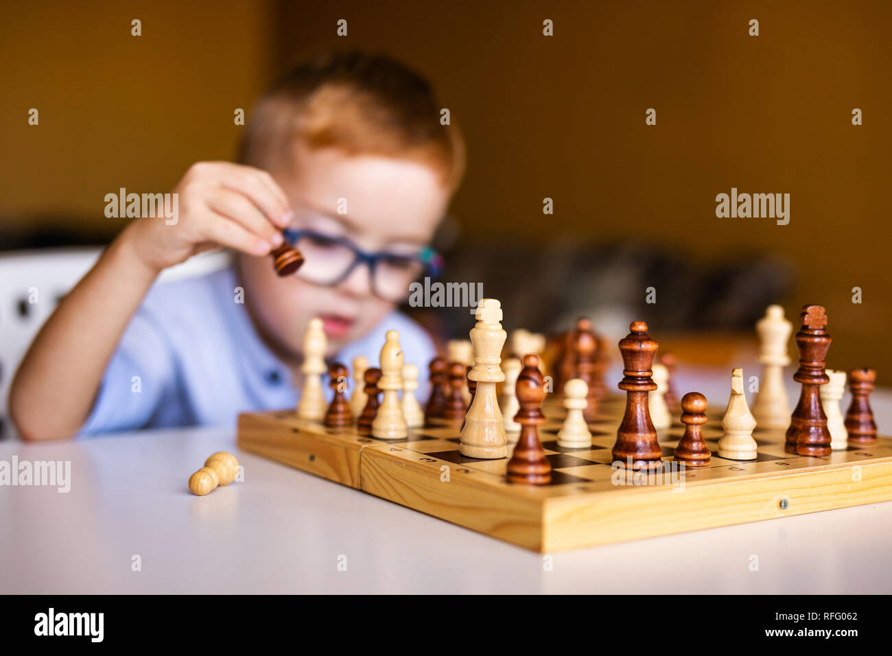 Ginger boy with down syndrome with big glasses playing chess at home ...