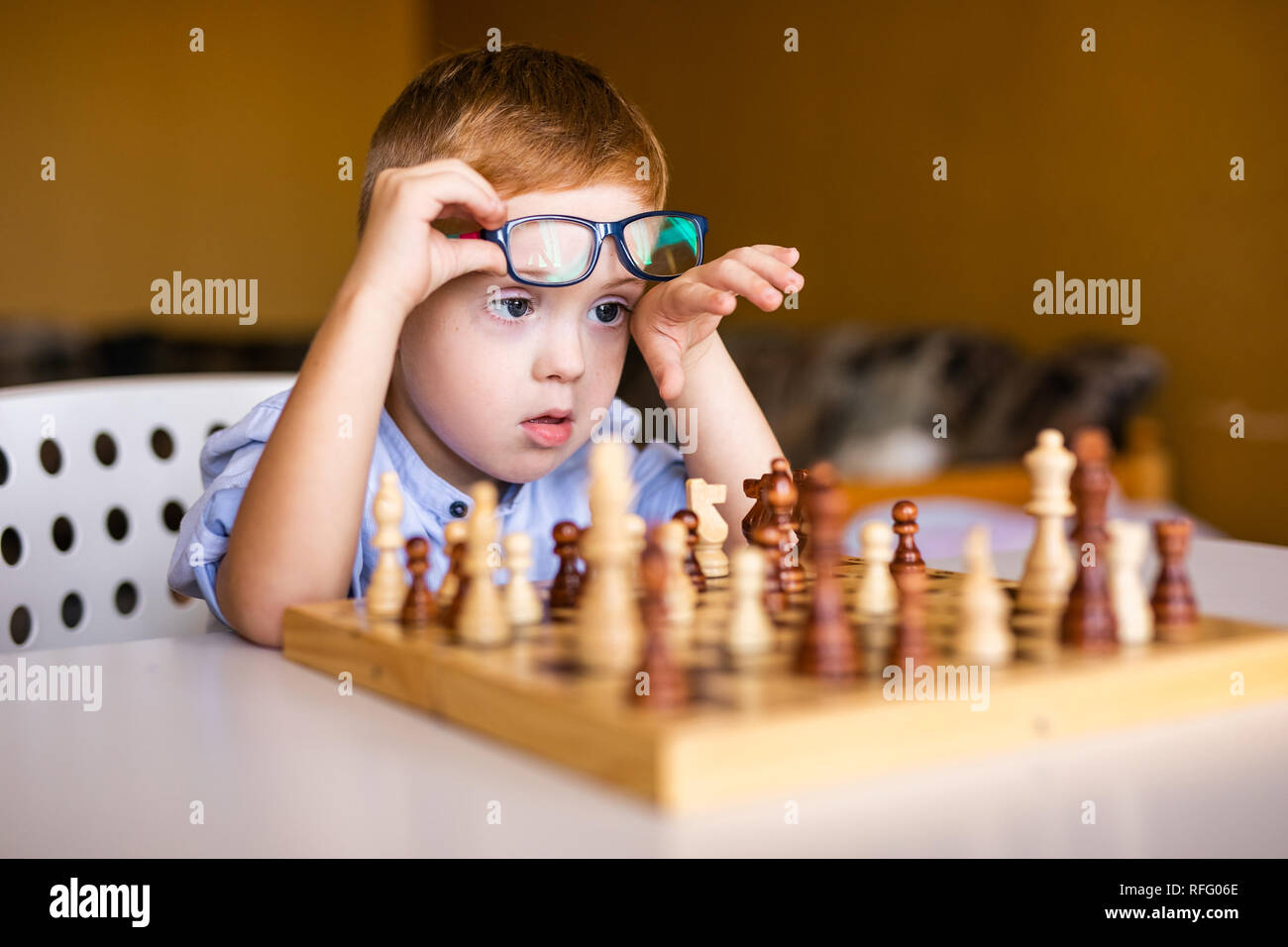 Ginger boy with down syndrome with big glasses playing chess at home ...