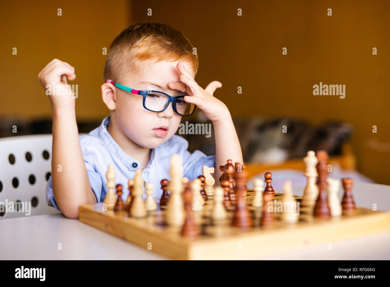 Ginger boy with down syndrome with big glasses playing chess at home ...