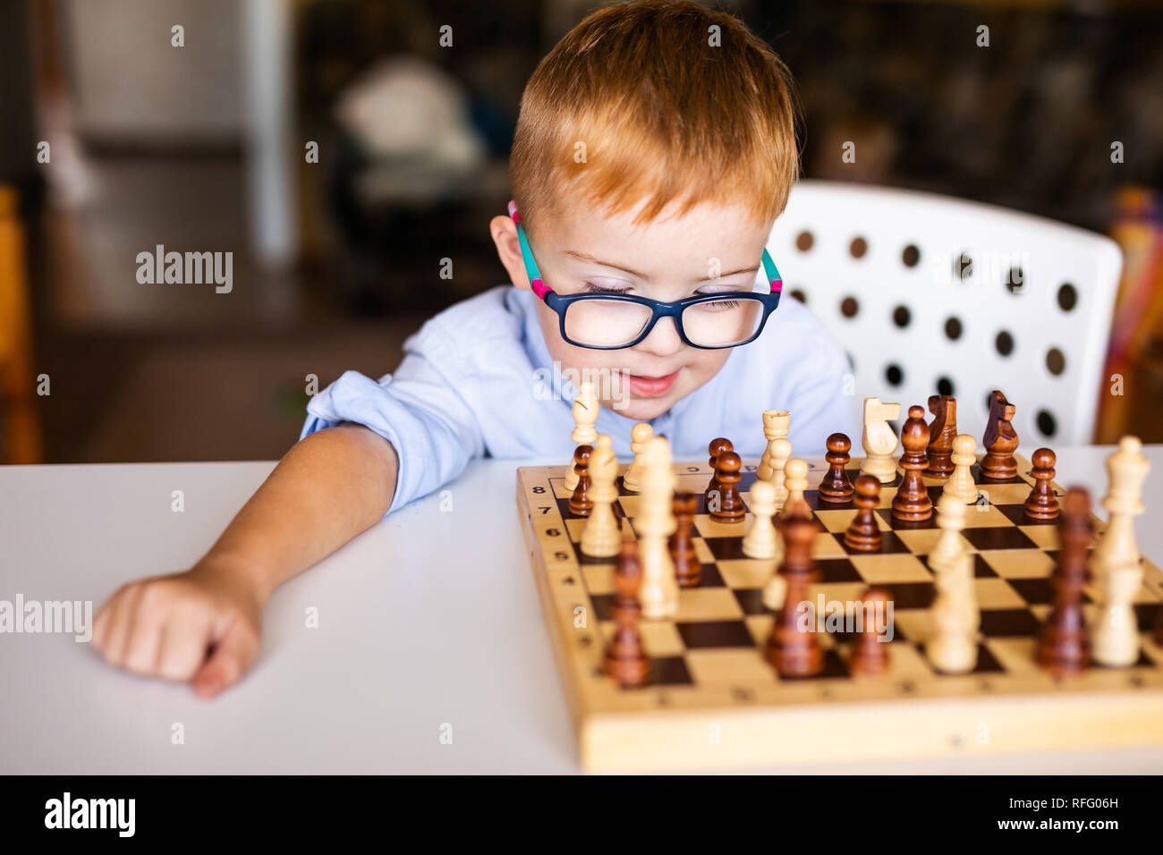 Ginger boy with down syndrome with big glasses playing chess at home ...