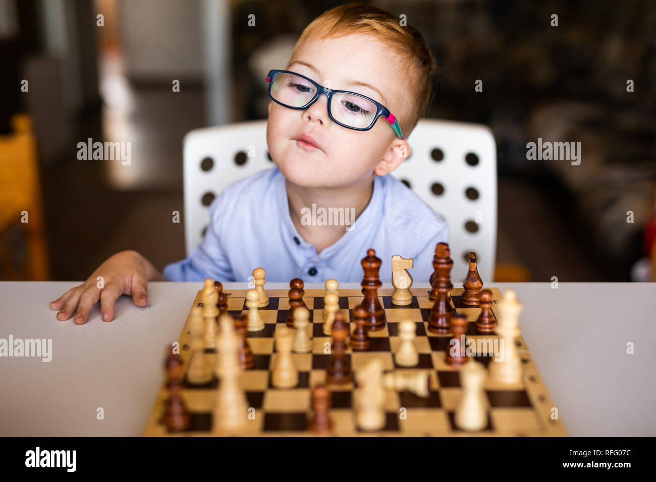 Ginger boy with down syndrome with big glasses playing chess at home ...