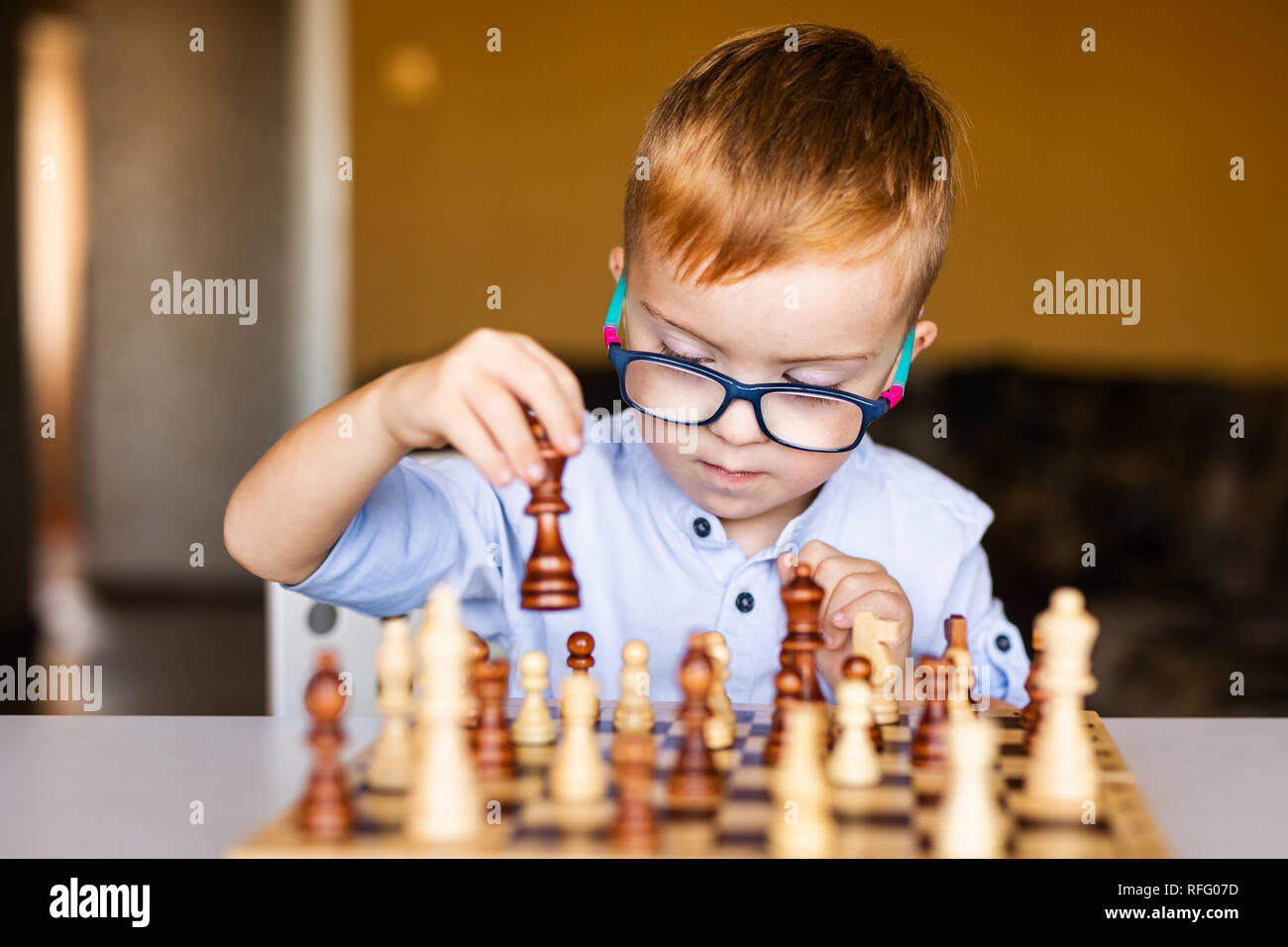 Ginger boy with down syndrome with big glasses playing chess at home ...
