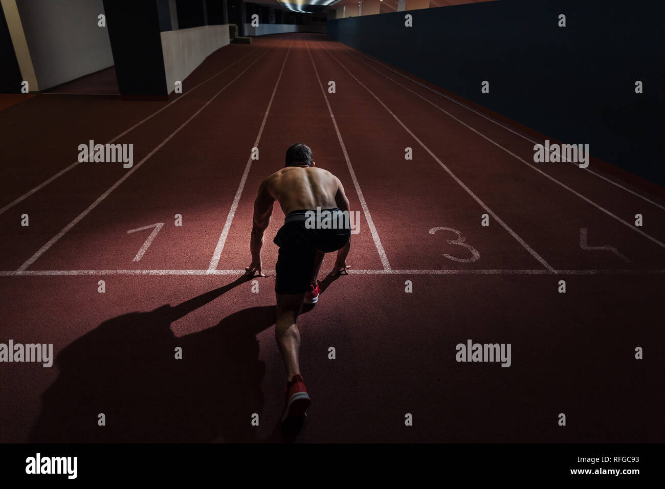 Very fit man on a an indoor track preparing to run in the start ...