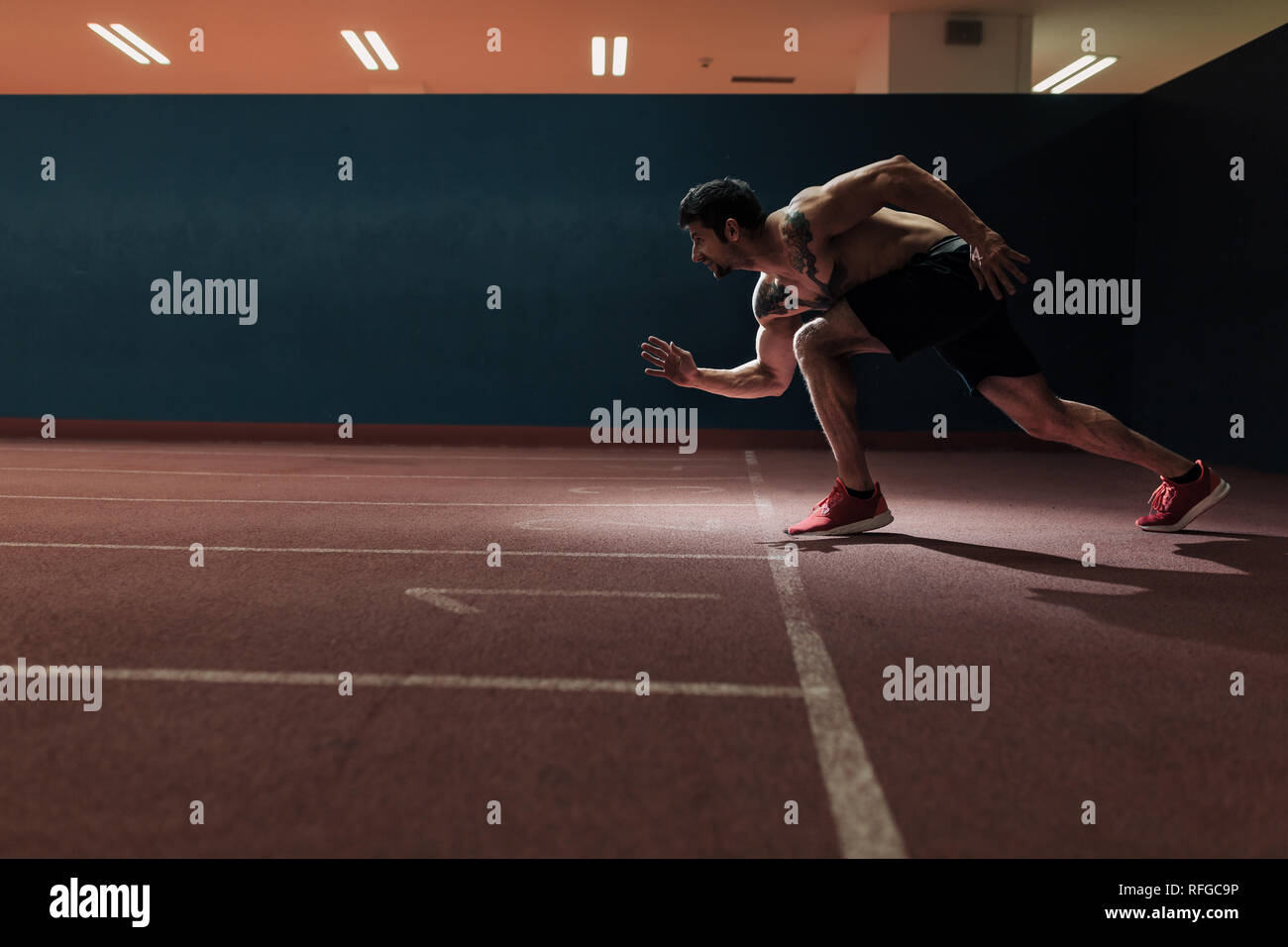 Very fit man on a an indoor track preparing to run in the start ...
