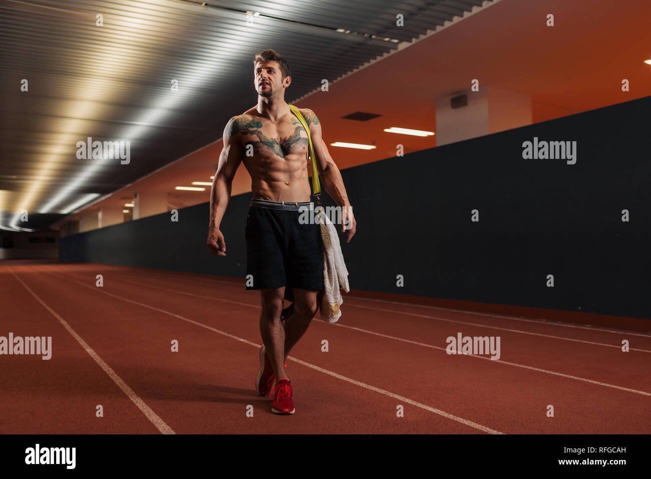 Fit man on an indoor track with a bag and workout and running equipment ...