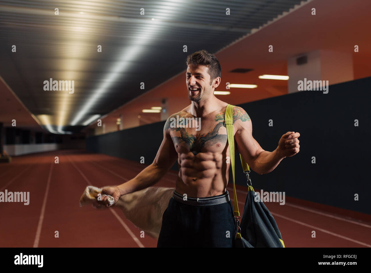 Fit man on an indoor track with a bag and workout and running equipment ...