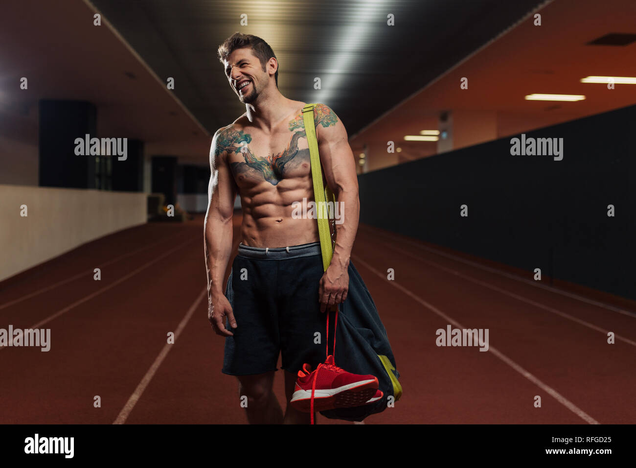 Fit man on an indoor track with a bag and workout and running equipment ...
