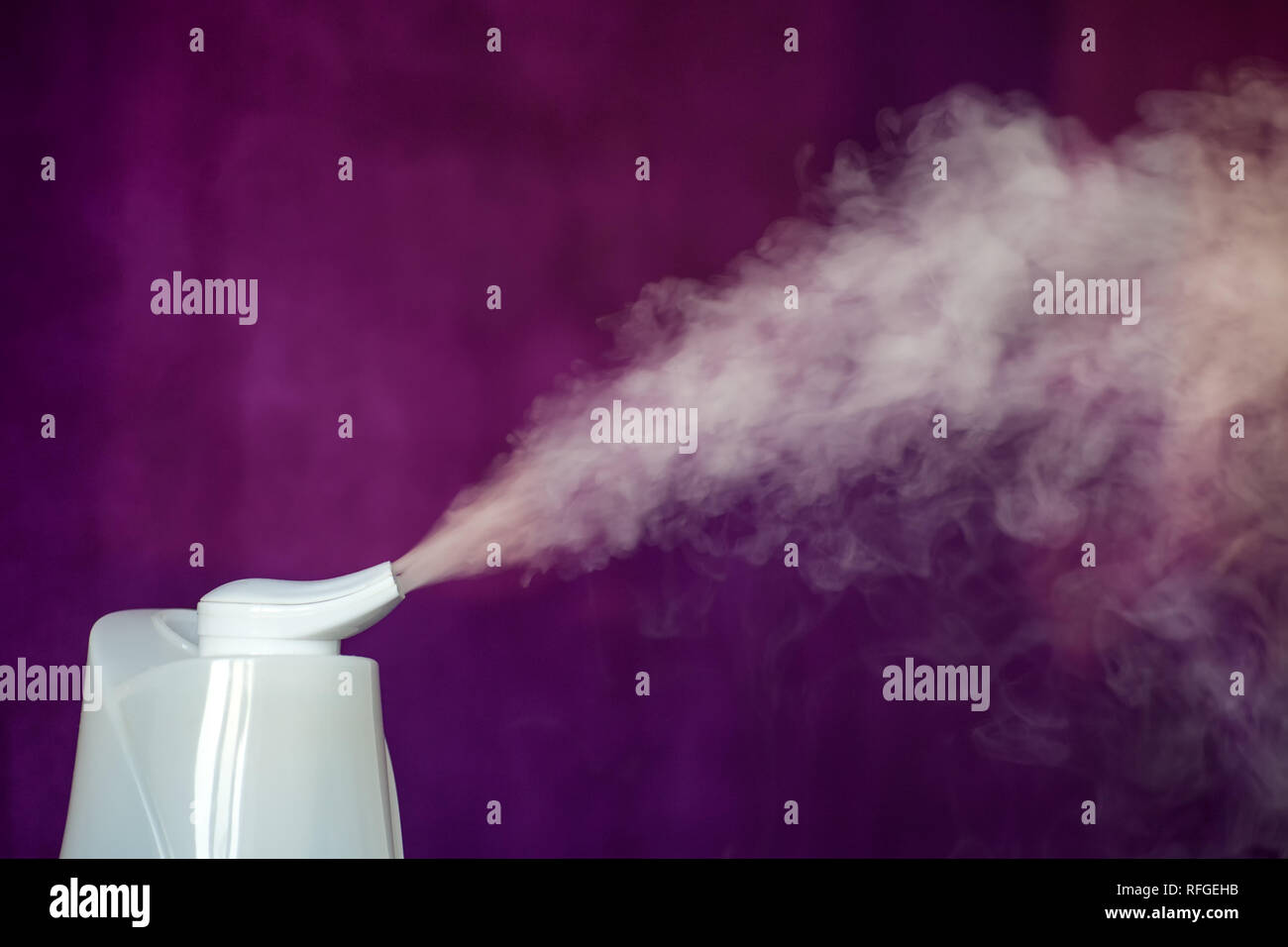 Humidifier spreading steam on purple background Stock Photo - Alamy