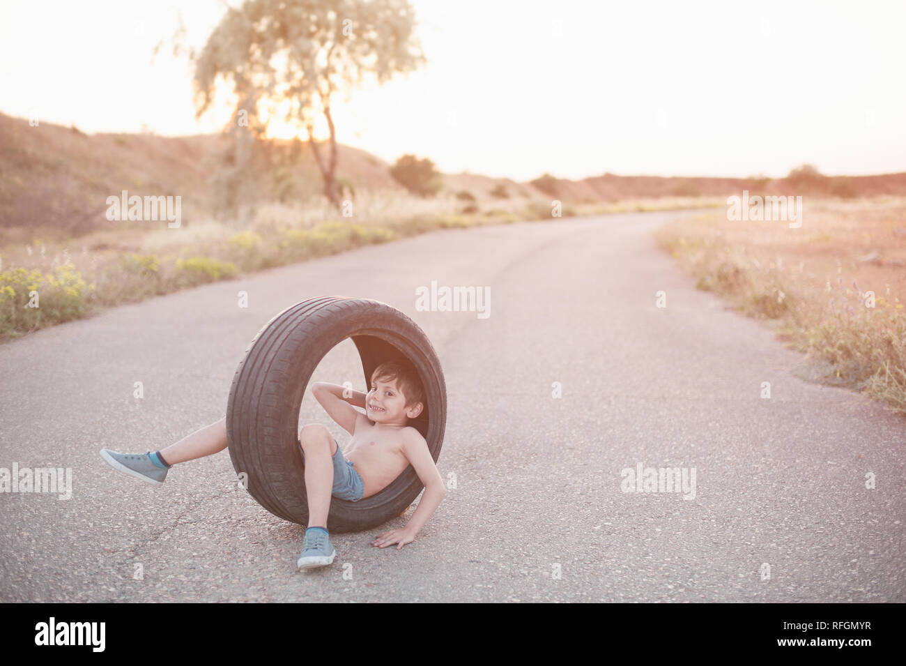 happy smiling caucasian small boy sitting inside car tire on empty ...