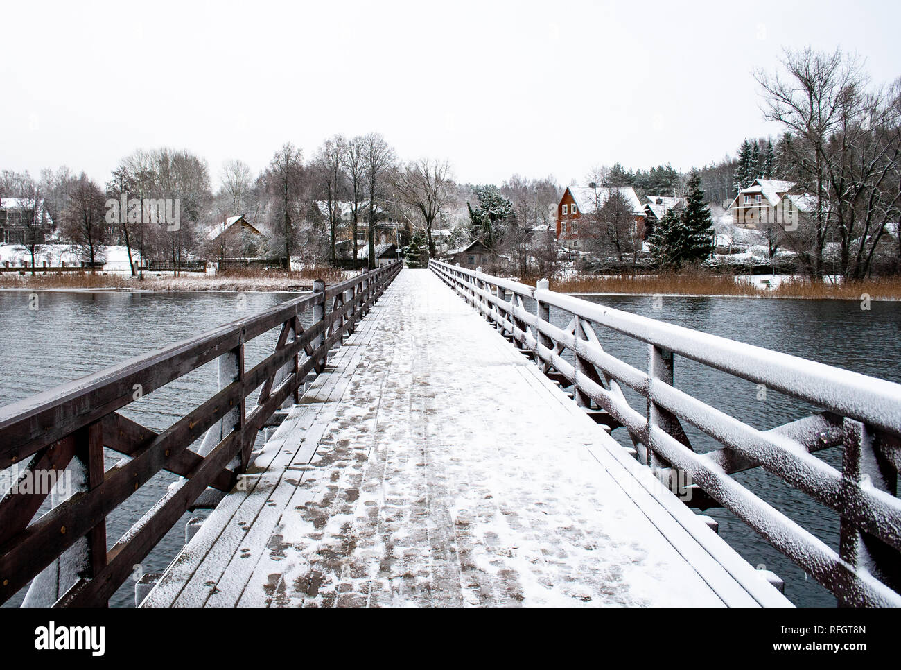 Wooden bridge in winter, trees and and wooden houses covered by snow in ...