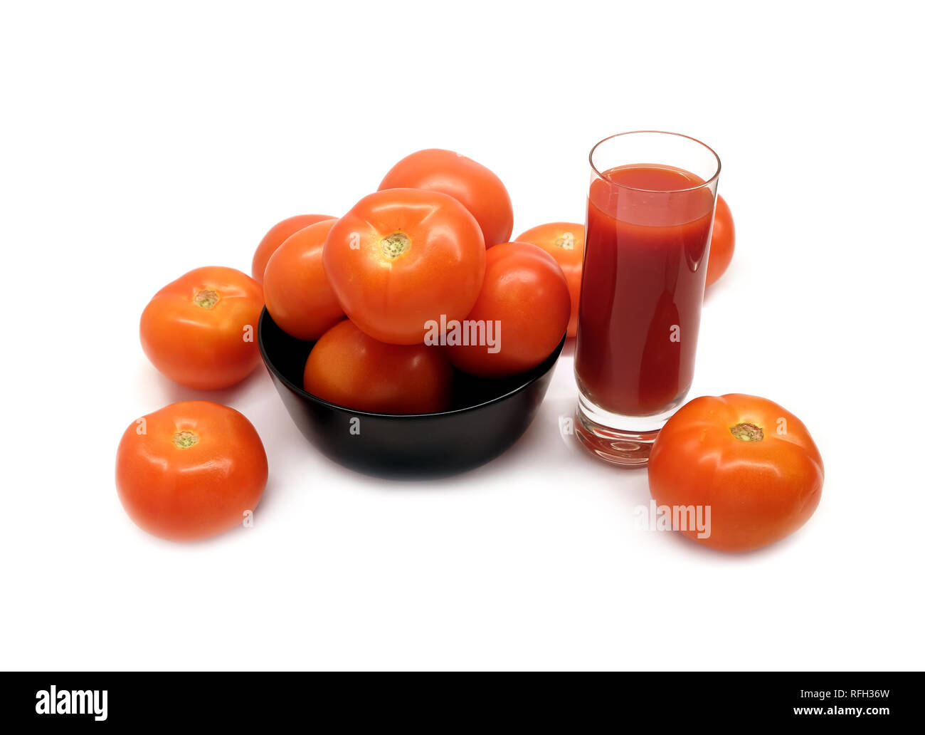 Big glass with tomato juice and many ripe tomatoes in round black bowl ...