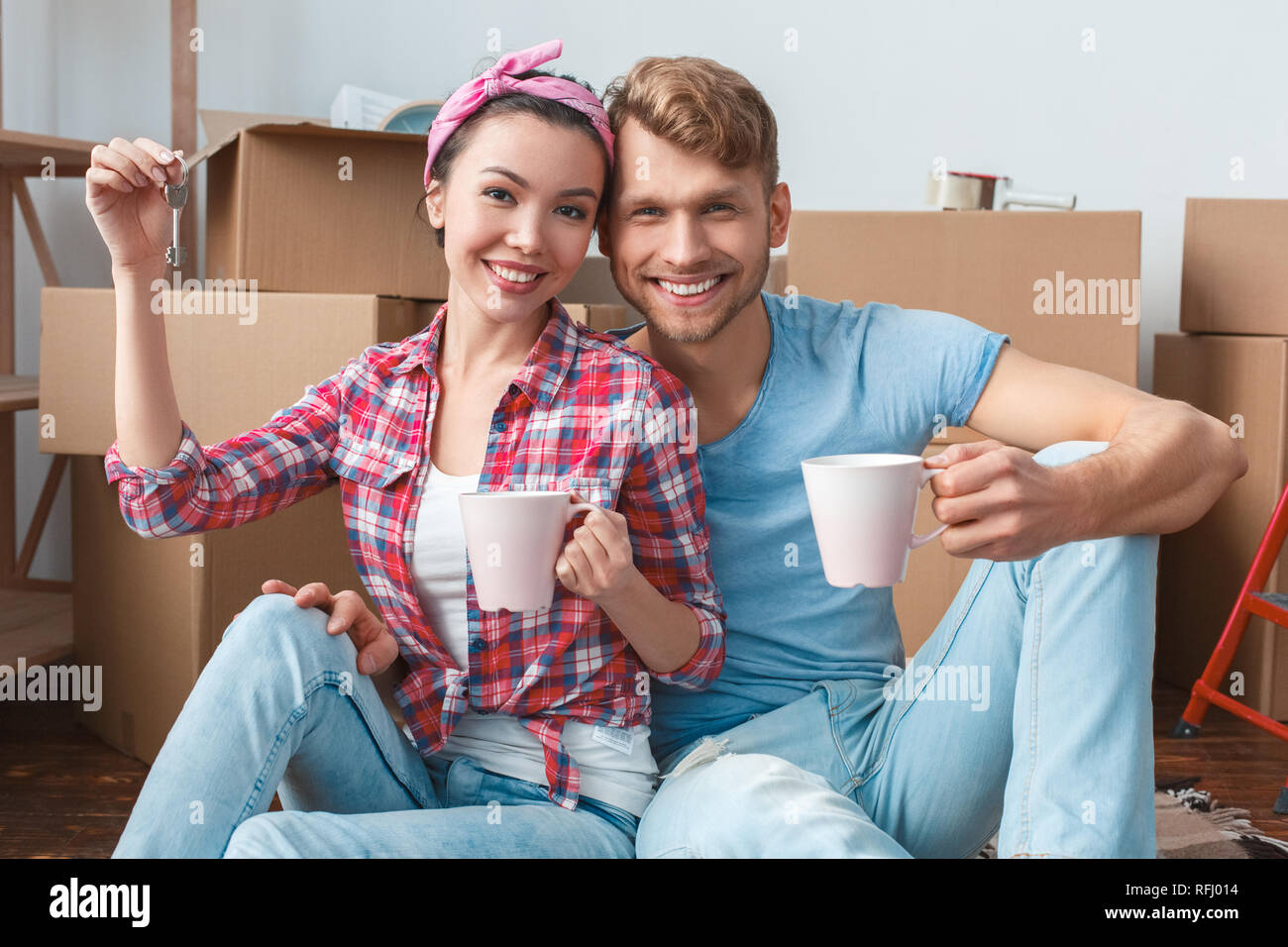 Young couple moving to new place sitting holding tea cups and keys ...