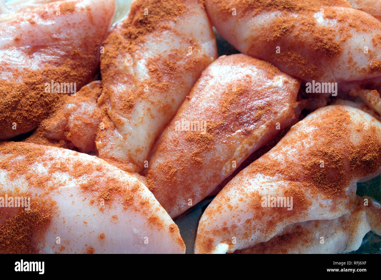 Many raw juicy sliced chicken pieces well sprinkled with red pepper ...