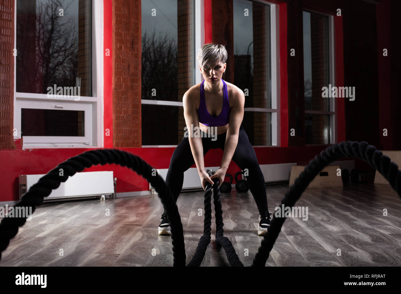 Fit and muscular woman exercising with battling ropes at fitness studio ...