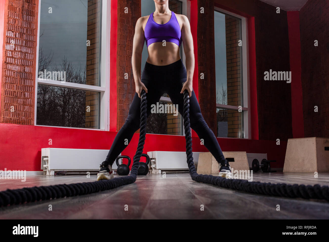 Fit and muscular woman exercising with battling ropes at fitness studio ...