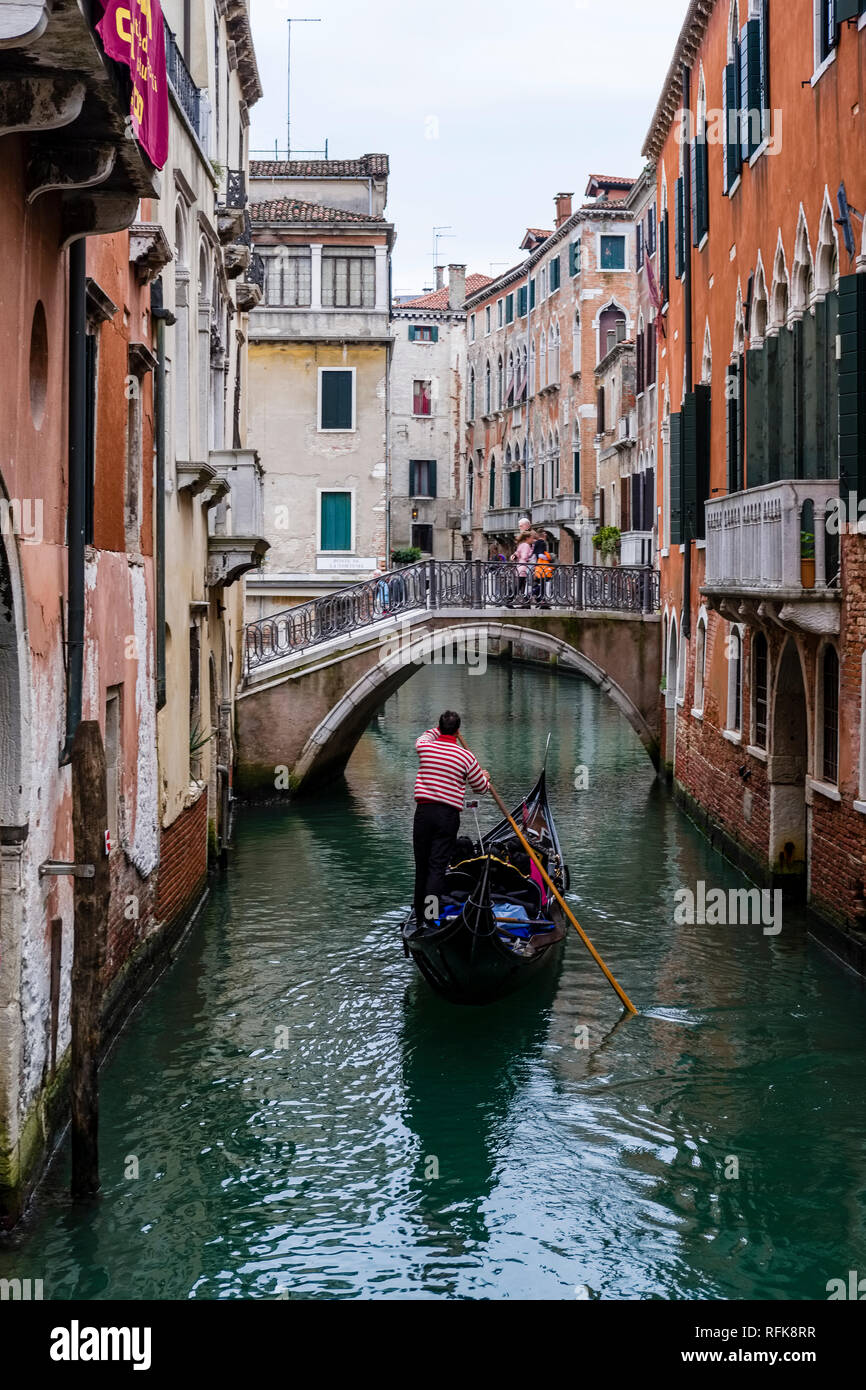 A Gondola, the traditional venetian rowing boat, is cruising on a small ...