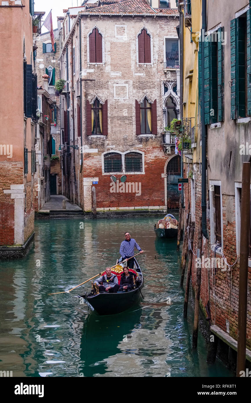 A Gondola, the traditional venetian rowing boat, is cruising on a small ...