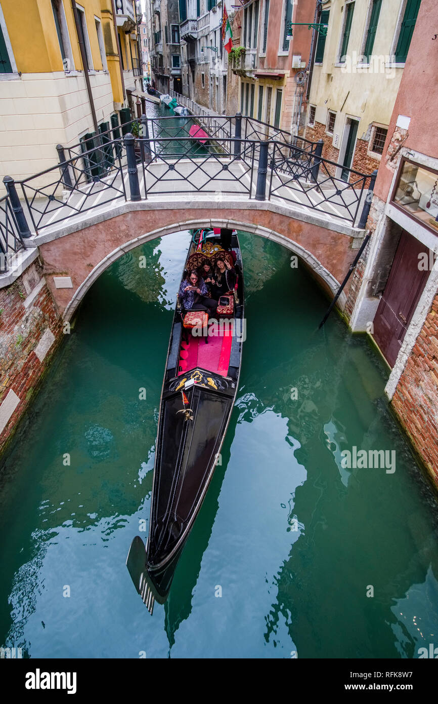 A Gondola, the traditional venetian rowing boat, is cruising on a small ...