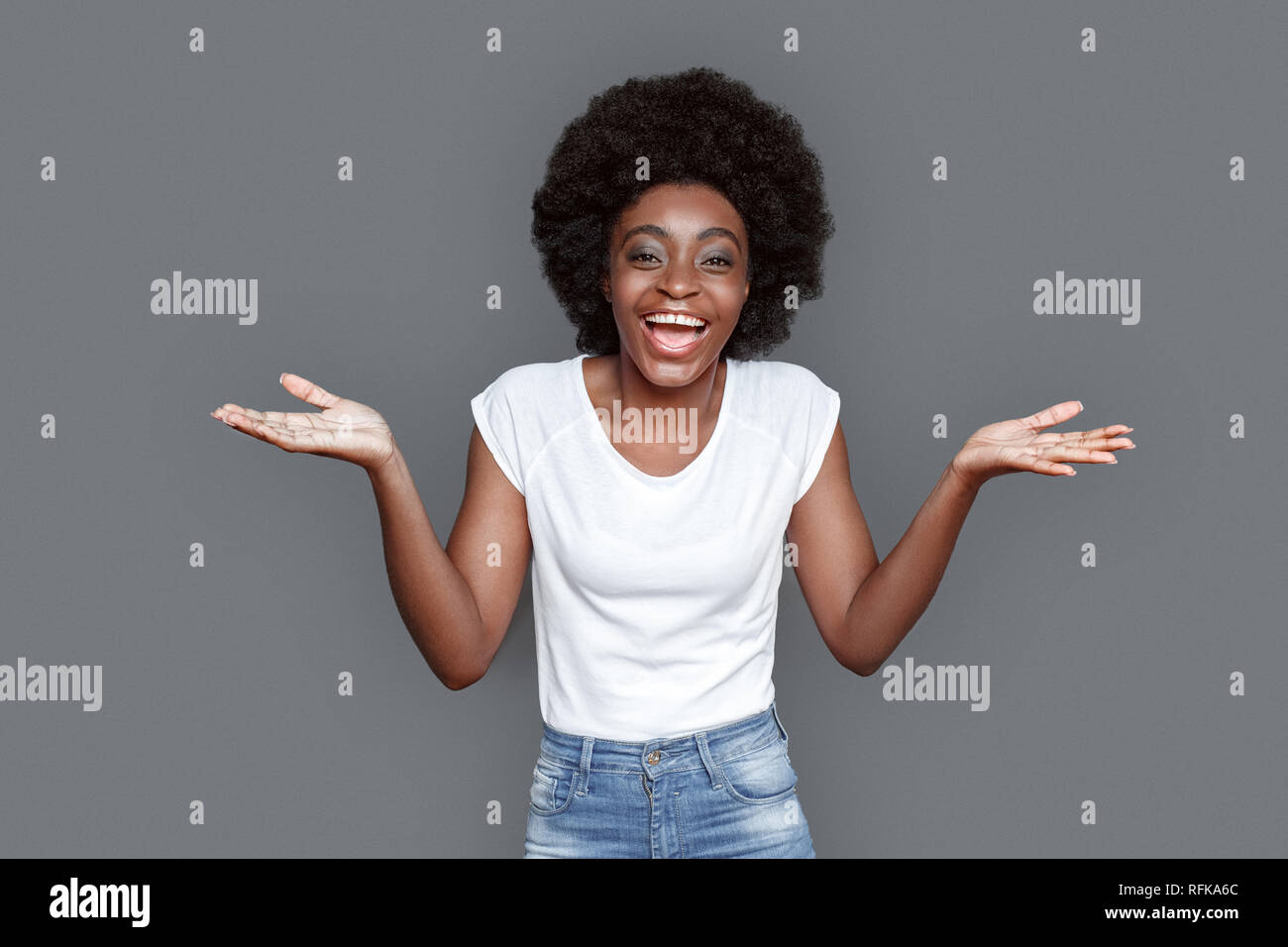 Young woman standing isolated on gray hands aside laughing confused ...