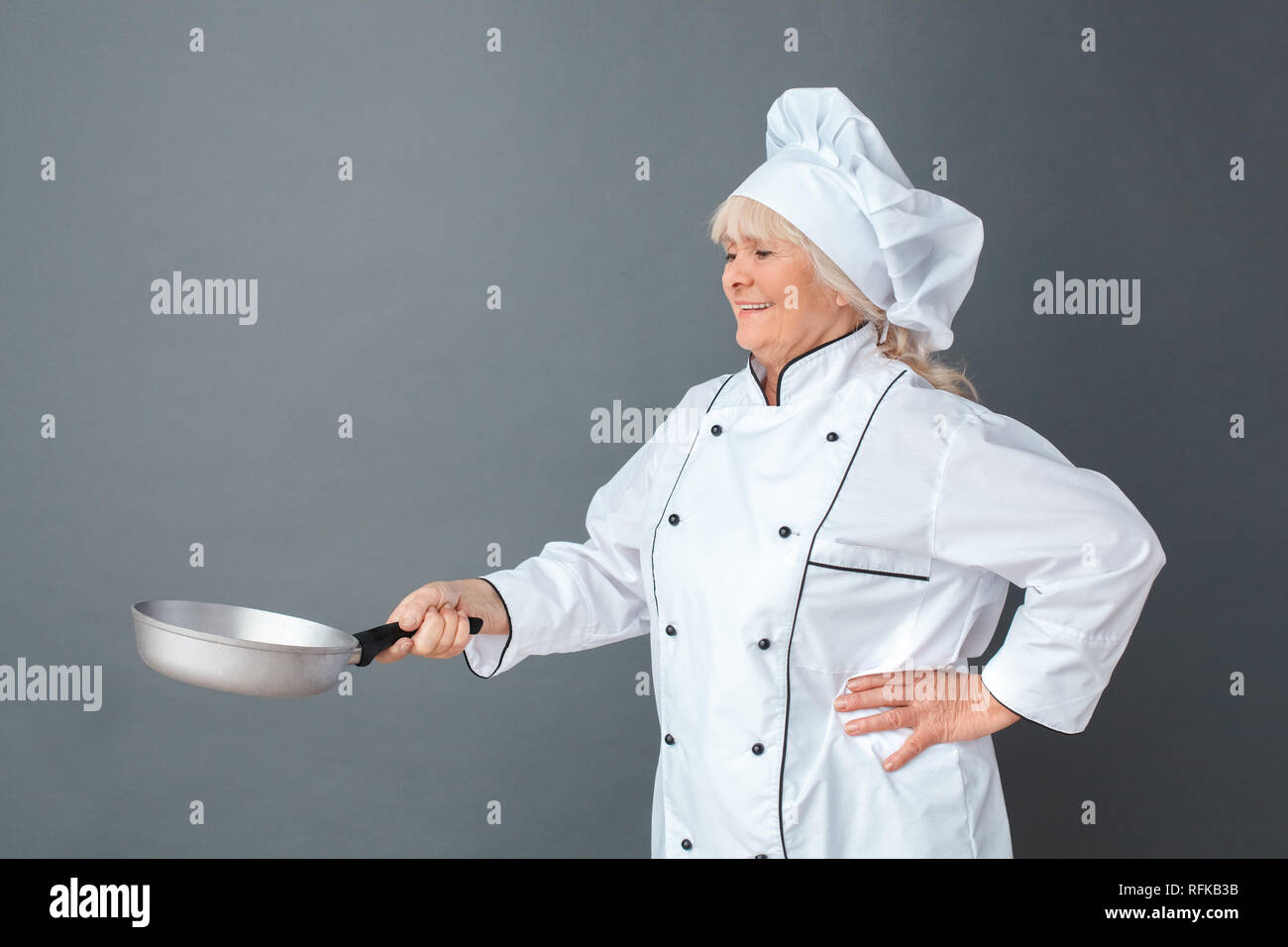 Senior woman chef studio standing isolated on gray with frying pan ...