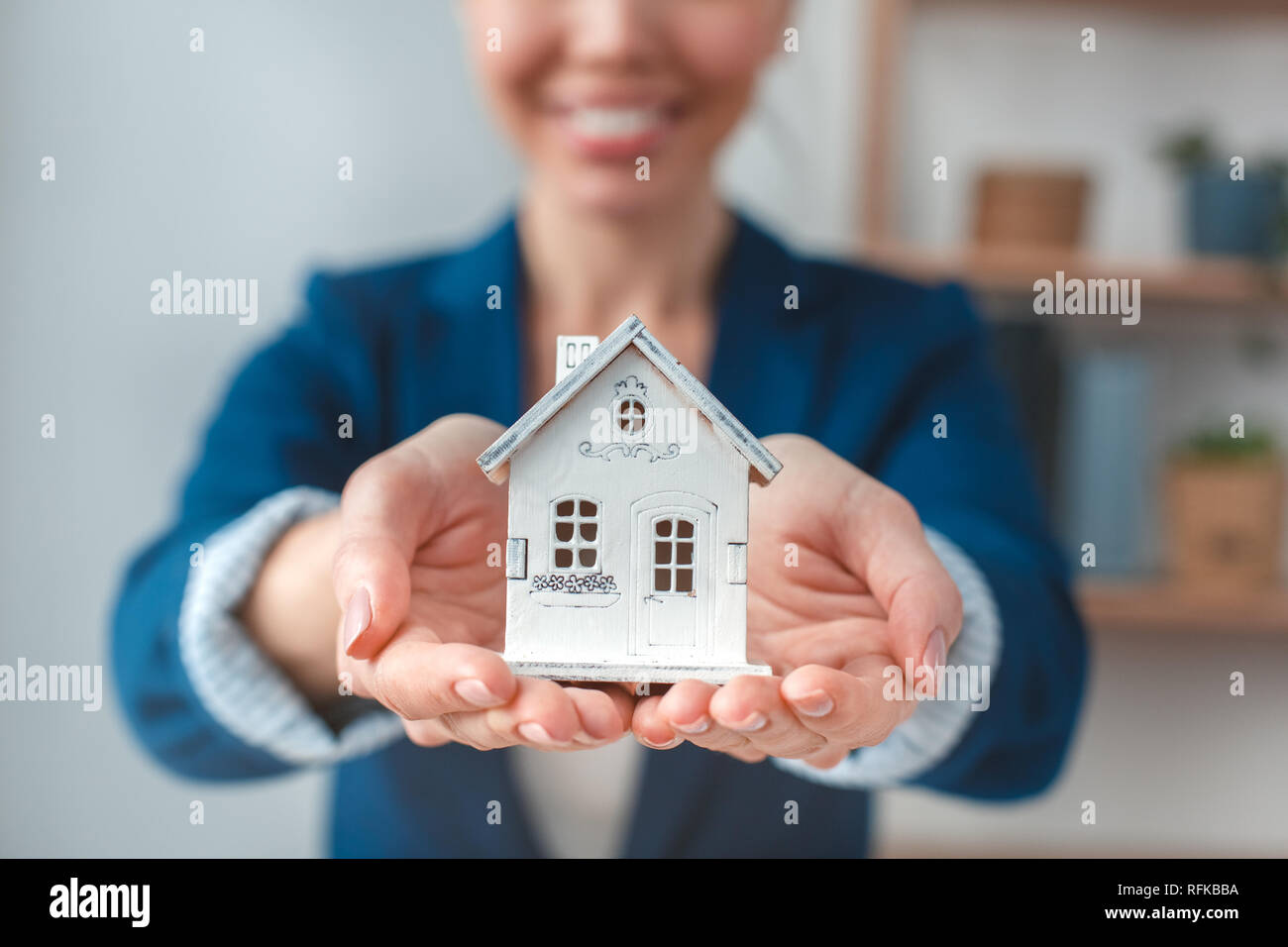Real estate agent at agency sitting holding house model close-up joyful ...