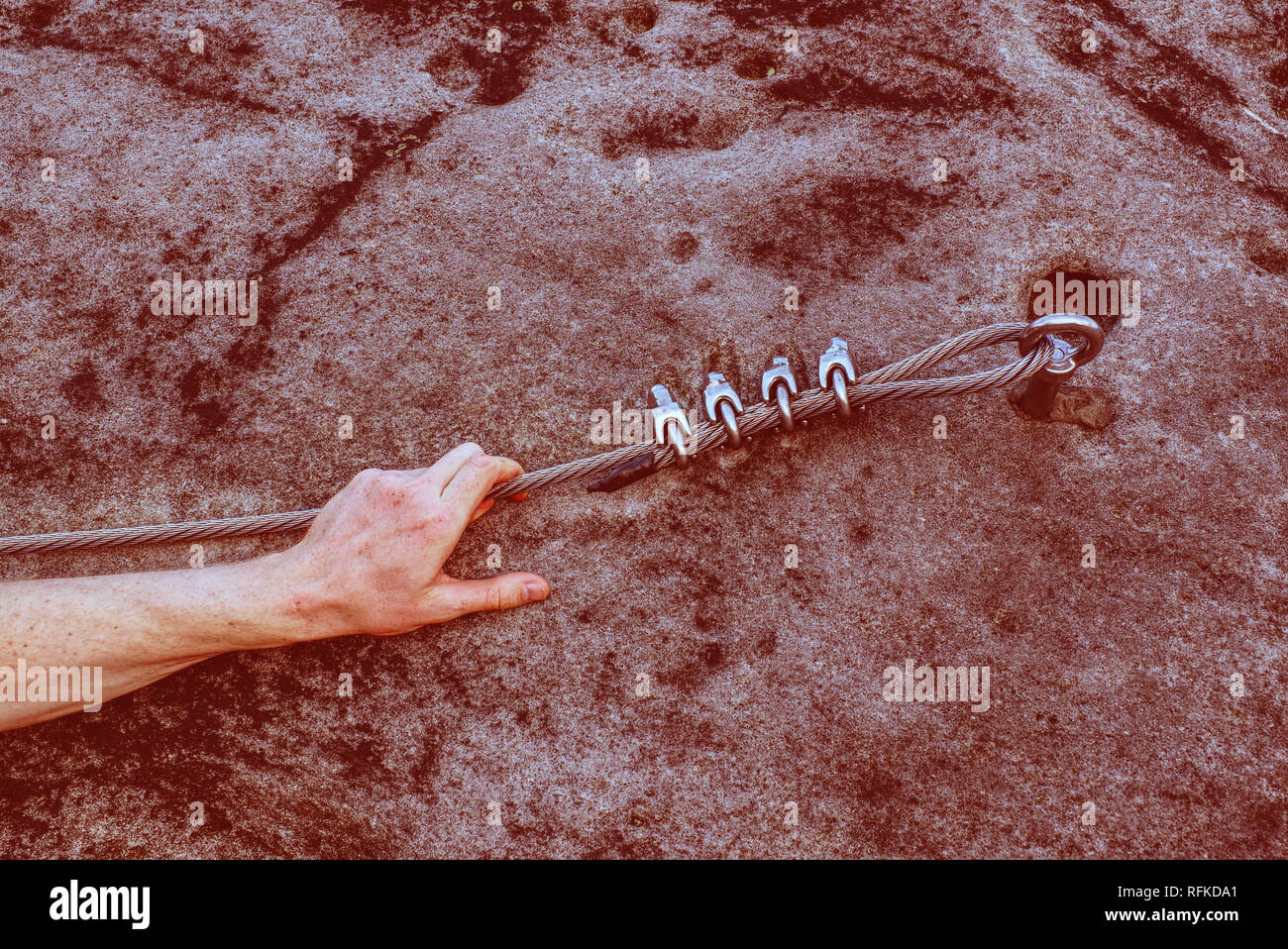 Rock climber's hand gripping metal rope at natural cliff in way via ...