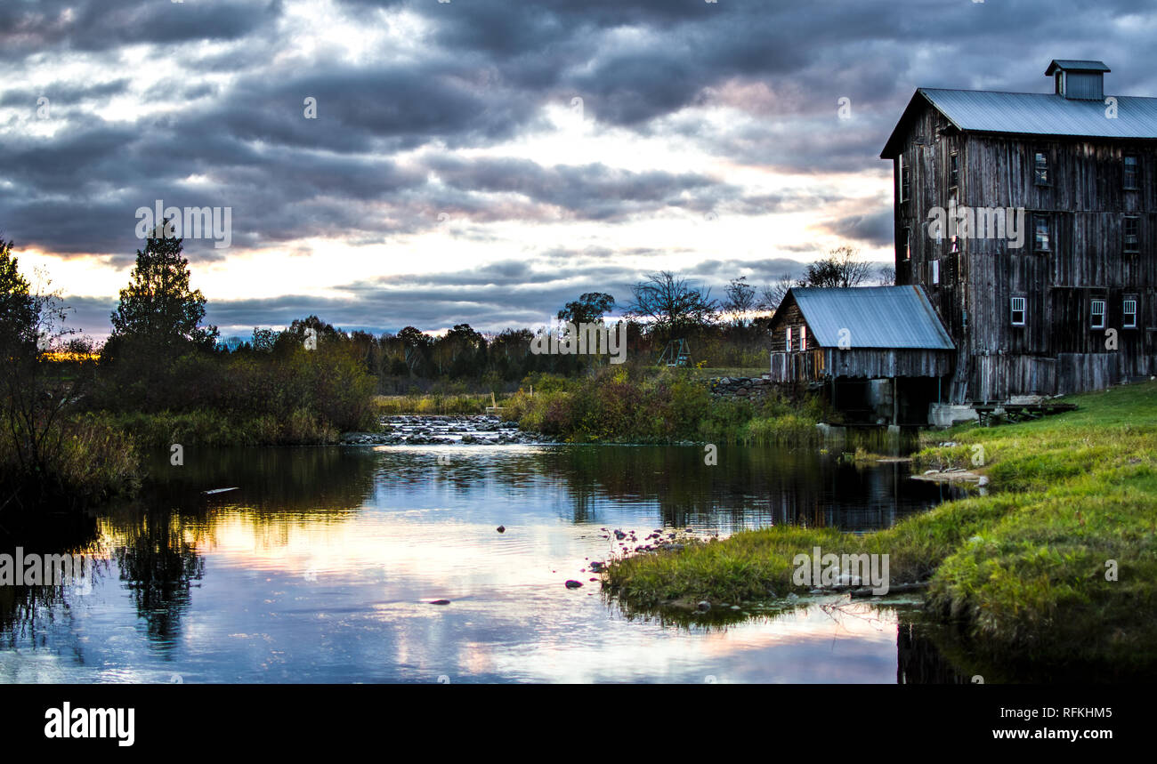 Old flour mill barn at the edge of a river just as the sunsets below ...