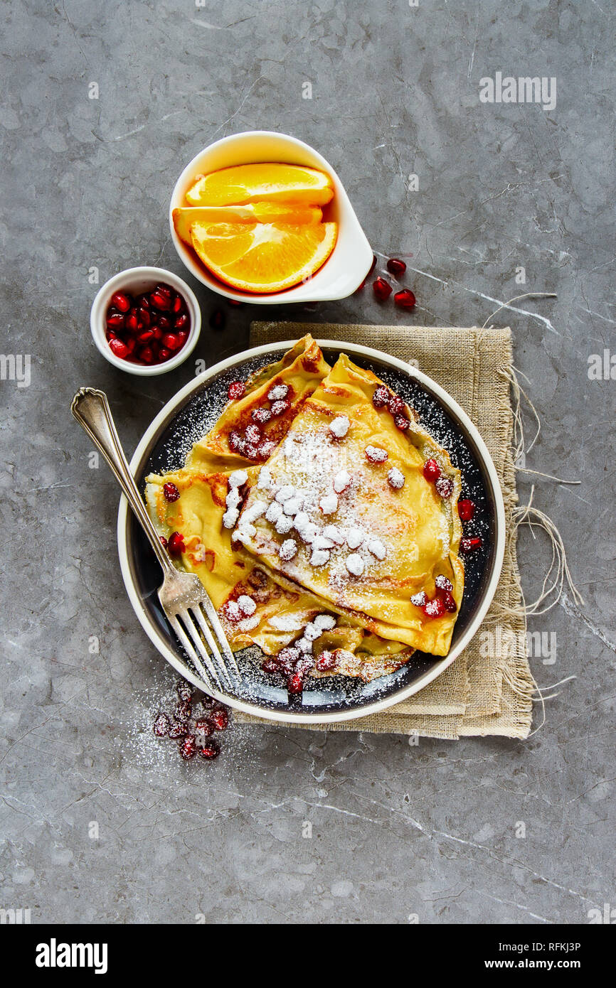 Flat lay of crepes in plate topped with pomegranate and sugar. Homemade ...