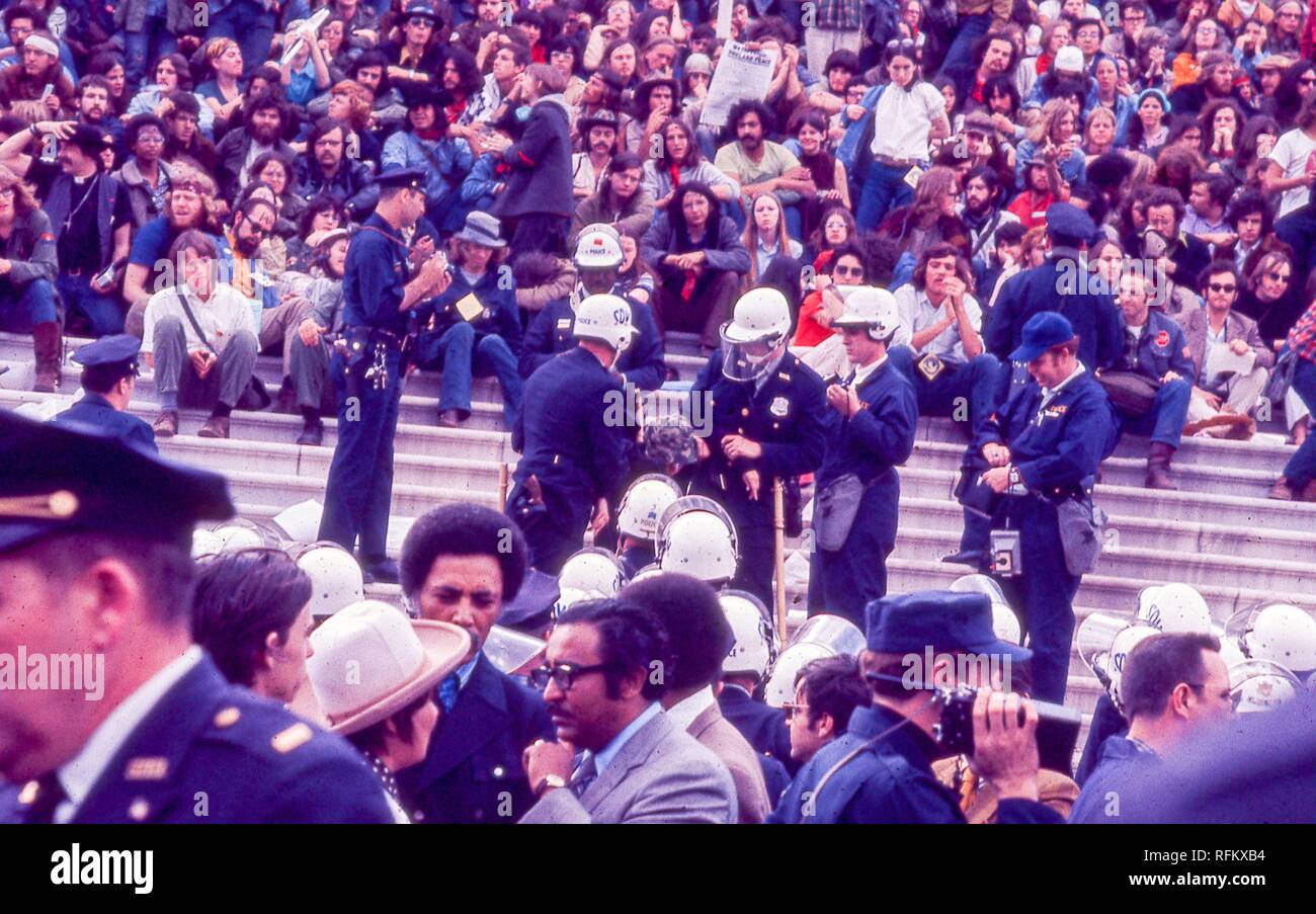 Police officers carry off protesters in hippie attire from a large ...