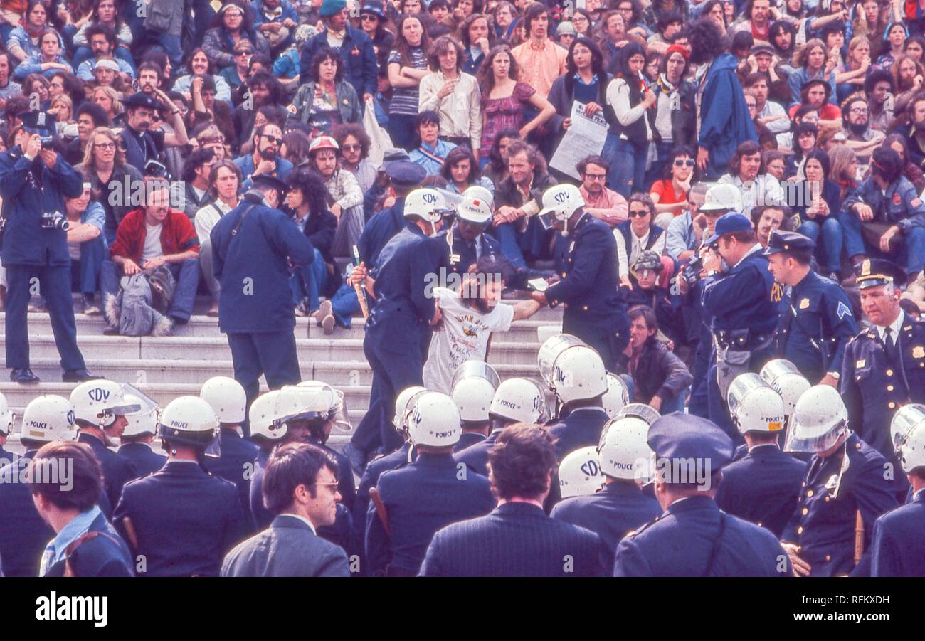 Police officers carry off protesters in hippie attire from a large ...