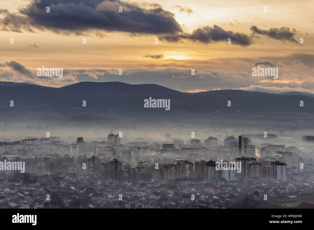 Distant city covered by mist and beautiful colors of burning sunset sky ...