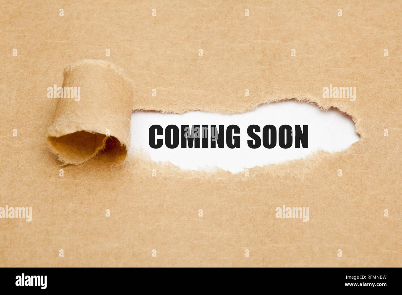 The phrase Coming Soon appearing behind ripped brown paper. Concept ...