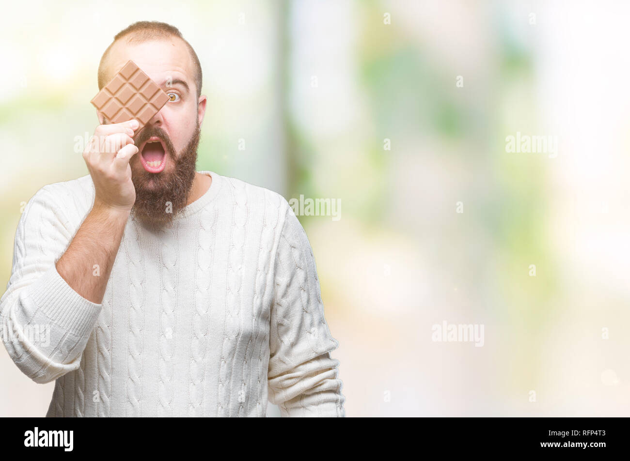 Young hipster man eating chocolate bar over isolated background scared ...