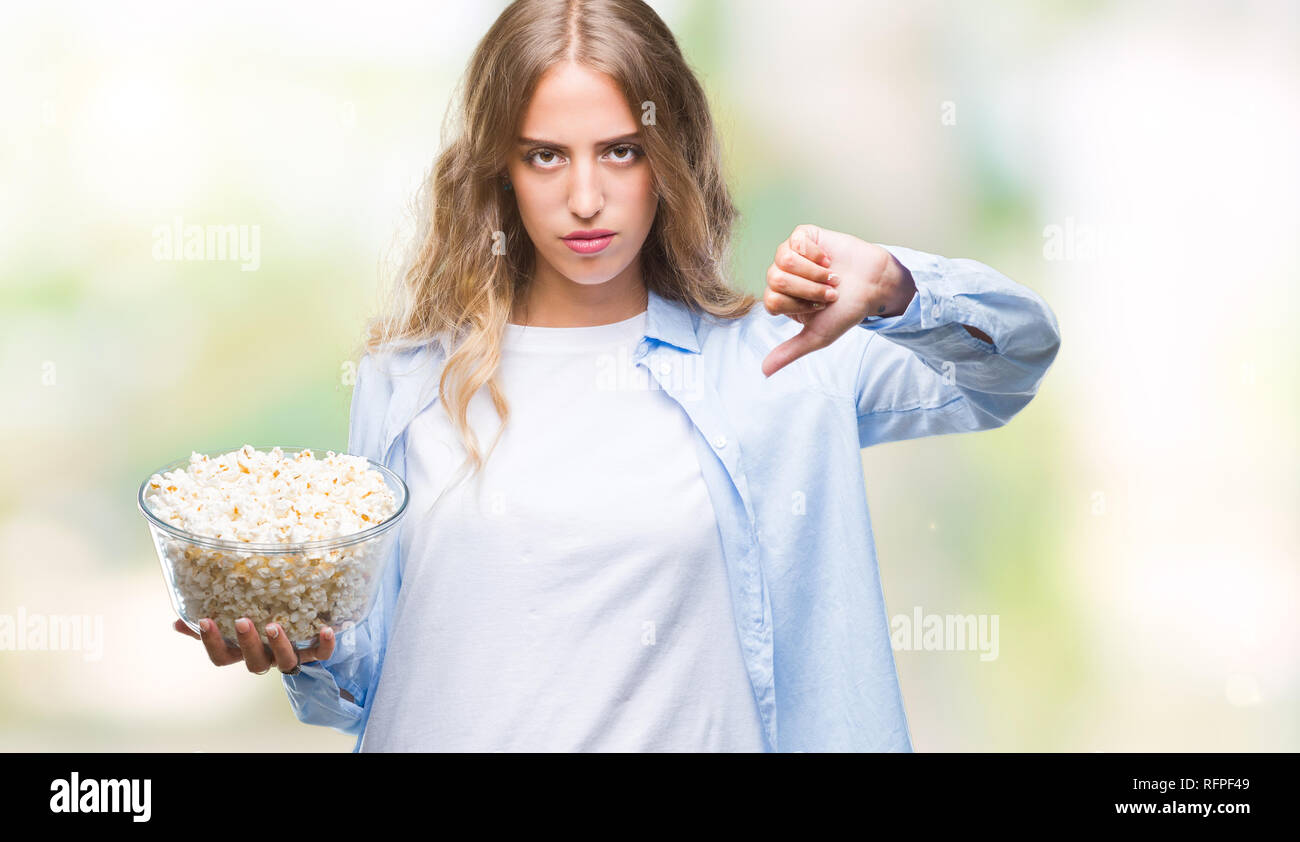 Beautiful young blonde woman eating popcorn over isolated background ...