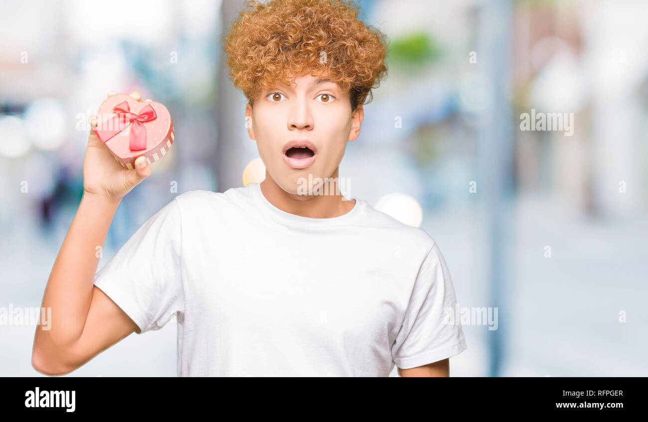 Young handsome man holding heart box as gift of valentine's day scared ...