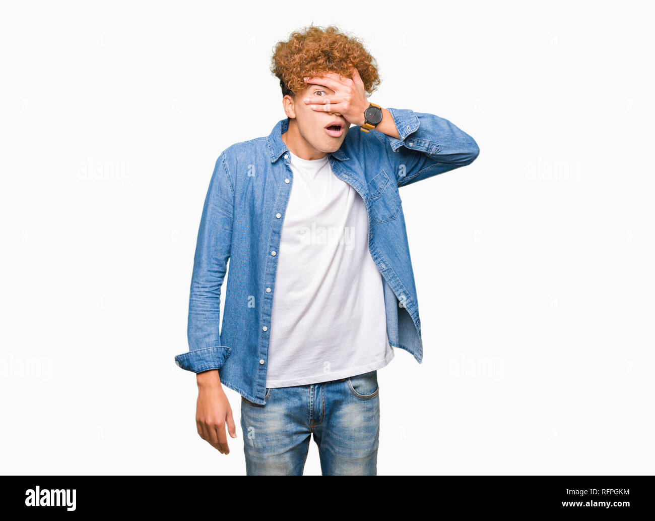 Young handsome man with afro hair wearing denim jacket peeking in shock ...