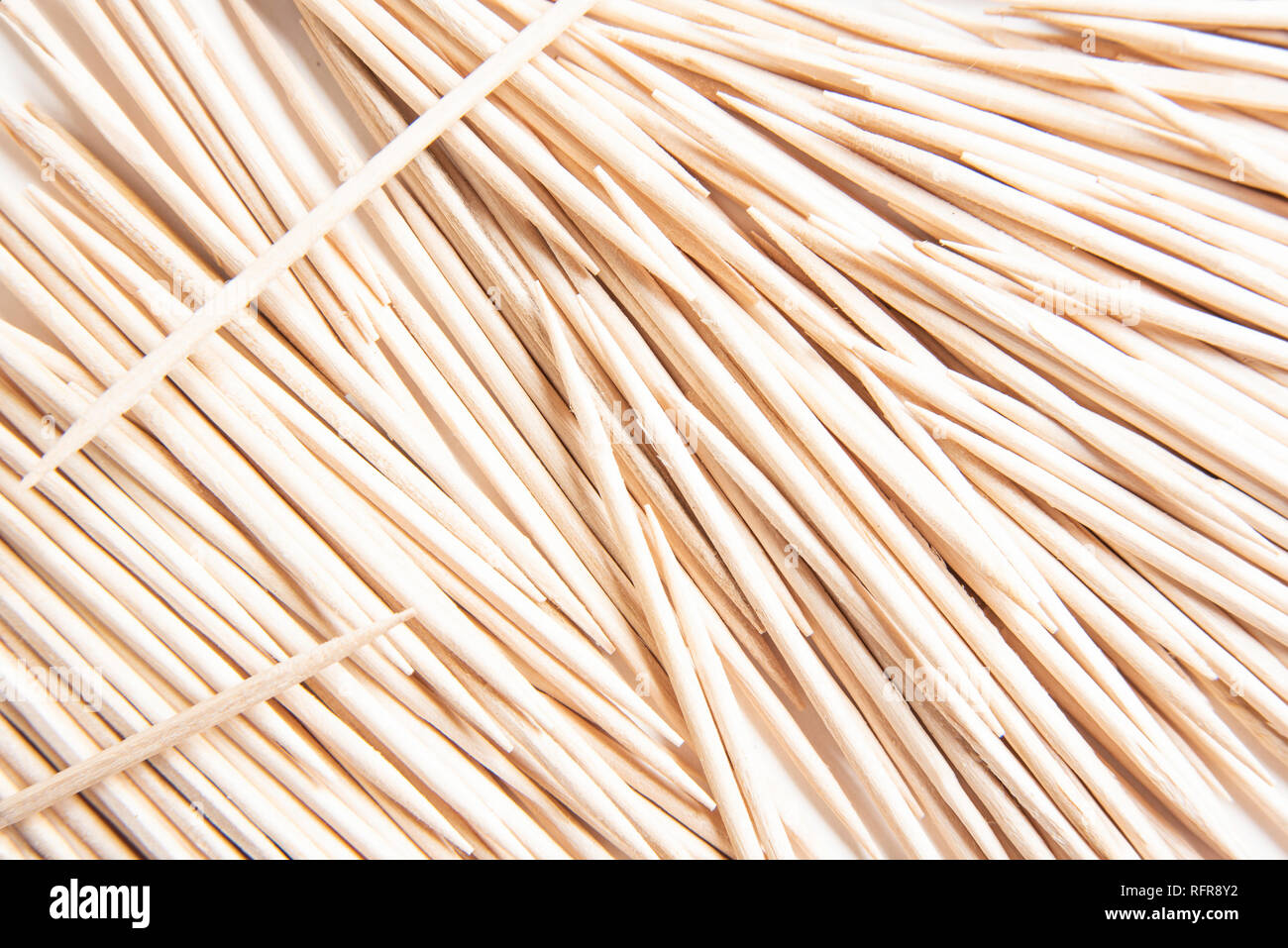 A bunch of unused round wooden toothpicks artfully scattered on a plain ...