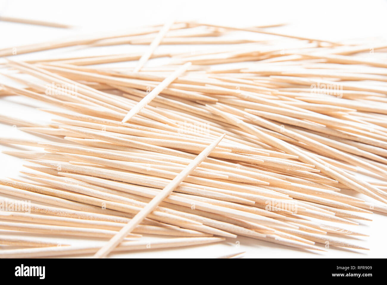 A bunch of unused round wooden toothpicks artfully scattered on a plain ...