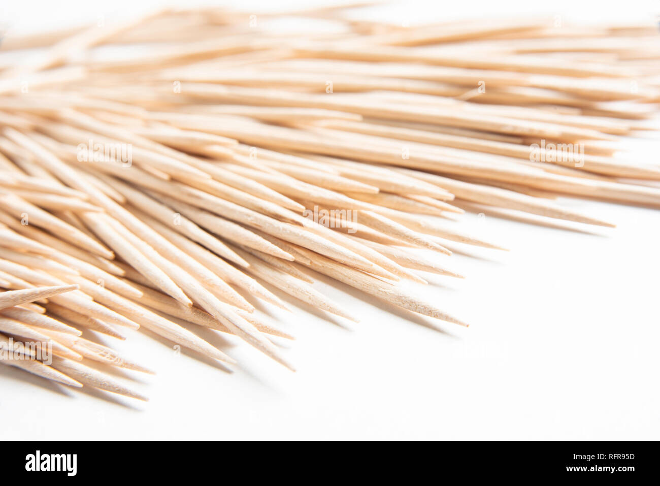 A bunch of unused round wooden toothpicks artfully scattered on a plain ...