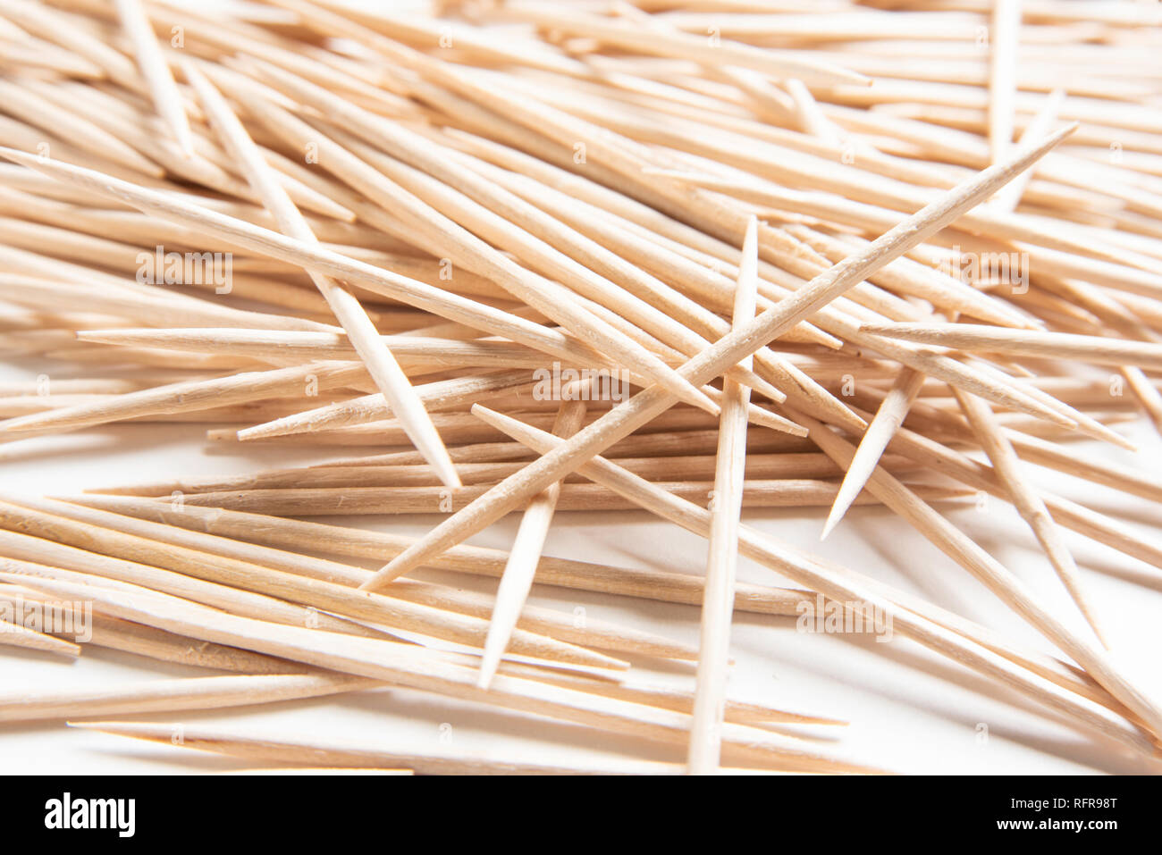 A bunch of unused round wooden toothpicks artfully scattered on a plain ...