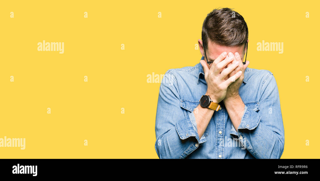 Handsome man wearing glasses with sad expression covering face with ...