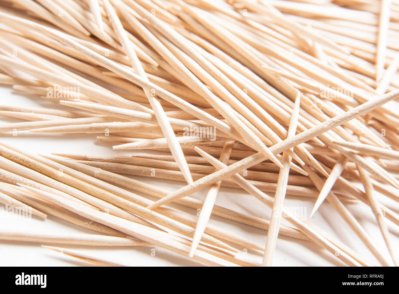 A bunch of unused round wooden toothpicks artfully scattered on a plain ...