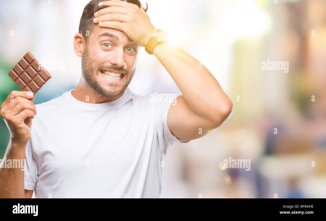 Young handsome man eating chocolate bar over isolated background ...